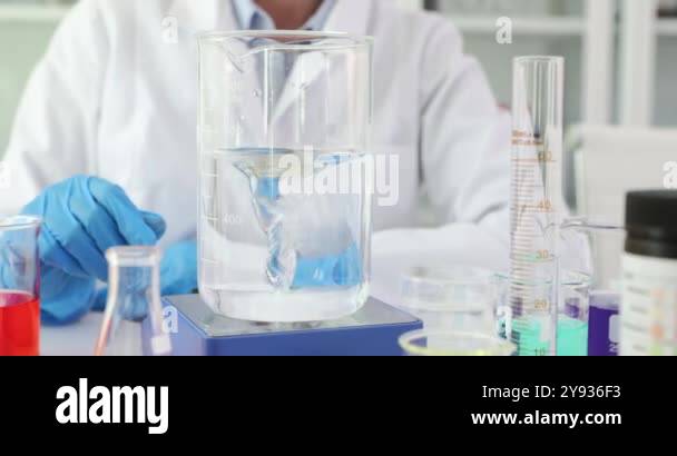 Scientist in uniform heats chemical liquid in beaker creating vortex. Laboratory worker prepares ...