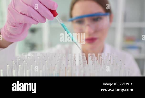 Woman chemist drips blue reagent liquid into glass test tubes in lab ...