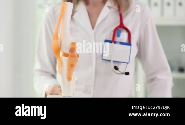 Doctor holding anatomical model of human knee joint and alarm clock in ...