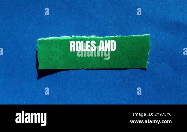 Roles and responsibilities message writing on ripped torn green paper piece on blue background ...