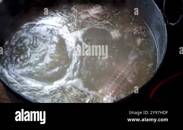 Close-up of meat boiling in a large pot as part of the traditional pig ...