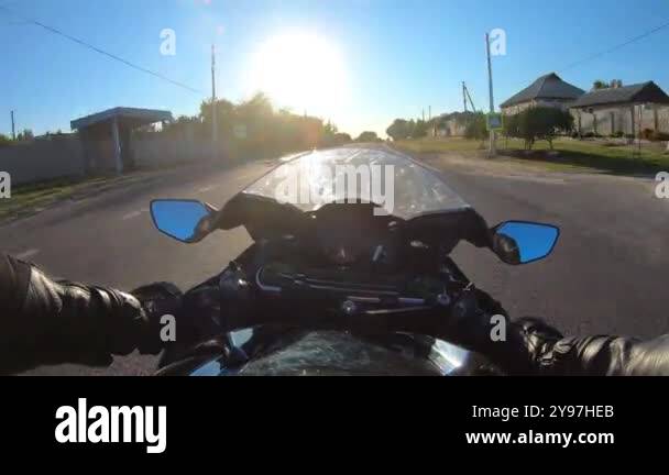 Point of view of a motorcycle rider rides in rural road through village ...