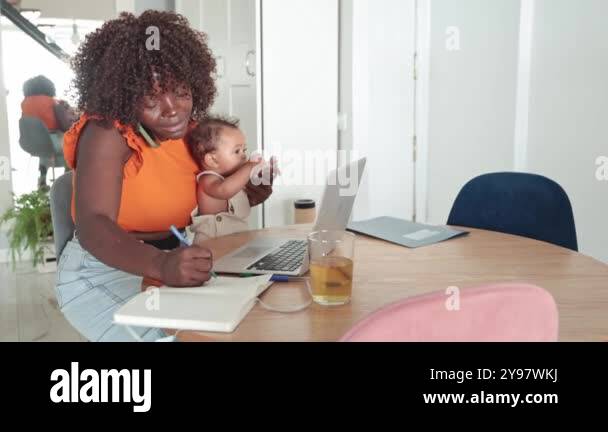 An African mother multitasks by talking on the phone, taking notes, and ...