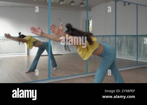 Side stretches with arms extended overhead in front of a mirror. Woman ...