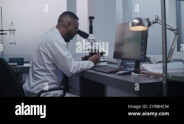 Medical science laboratory: African American microbiologist looks under ...