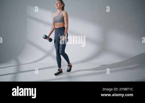 Sport trainer doing dumbbell squats at light studio. Strong woman with ...