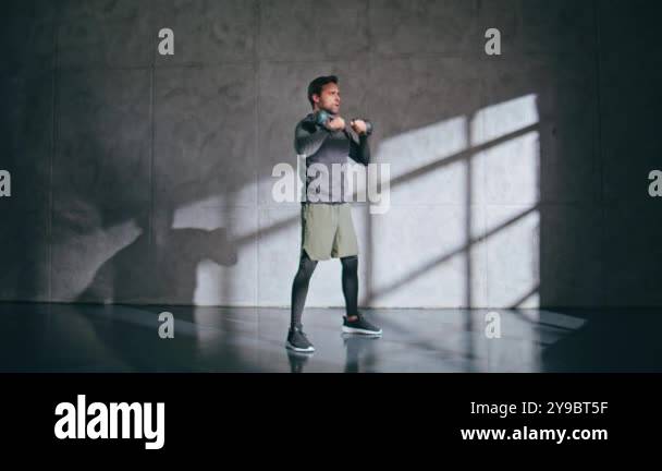 Strong bodybuilder lifting kettlebell making squat in gym. Healthy man ...