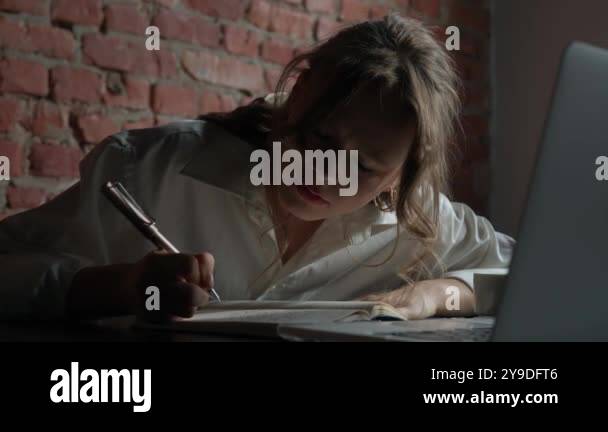 Female writing text on paper sheet. Business woman at office desk with laptop writing in dairy ...