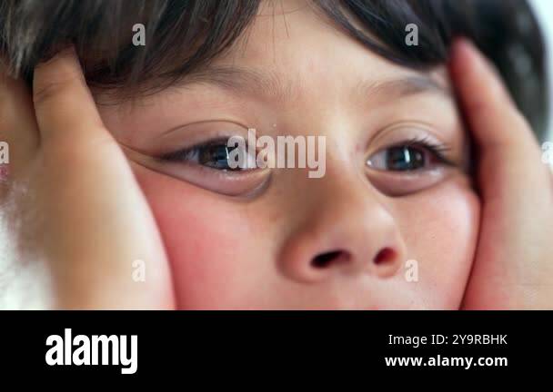Child pressing face into hands with a distant gaze, lips slightly ...
