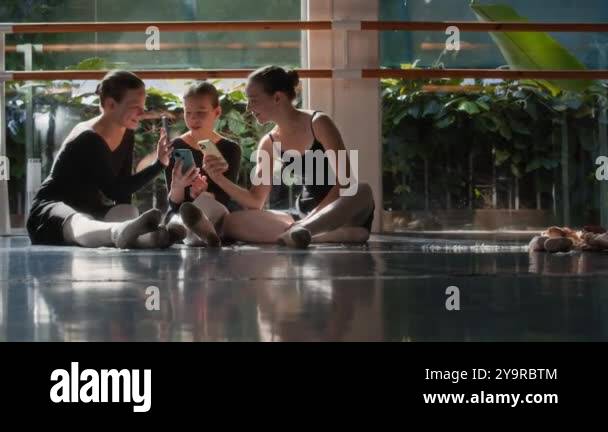 Three young ballet dancers in black leotards using their mobile phones ...