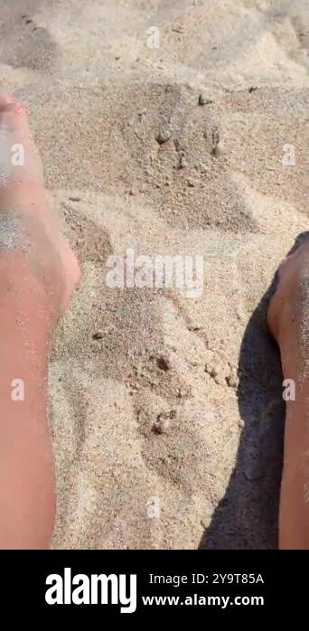Woman digging with feet in sand. Person playing burying his feet in dry sand on sandy beach on ...