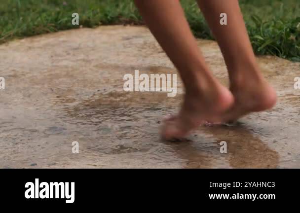 A child is jumping barefoot in a rainwater puddle in the backyard. The ...
