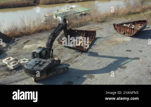 Above view, excavator pulls over ground part of old freight vessel's ...