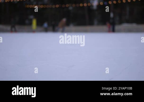 A skater glides across a snowy outdoor ice rink, creating splashes of ...