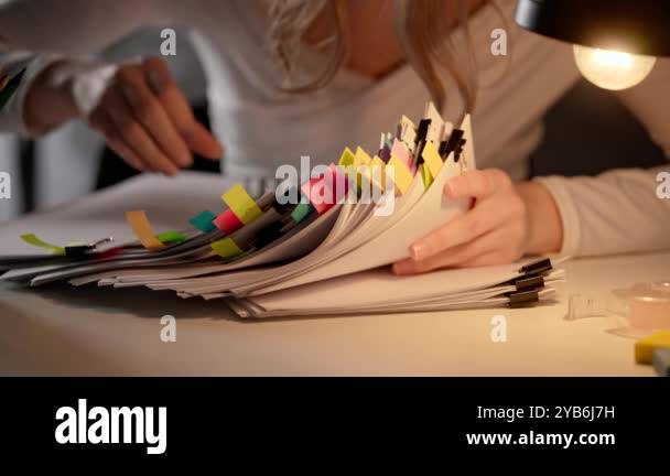 Female employee works with report papers. Workaholic woman at office desk sorting stack of paper ...