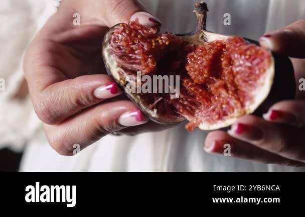 Woman opens fresh ripe fig, demonstrates juicy pulp inside fruit. Ficus ...
