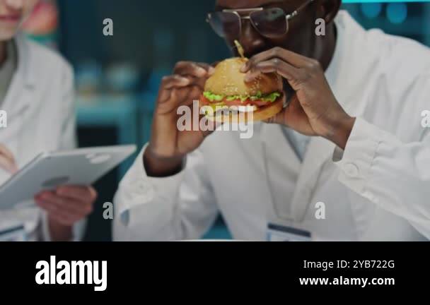 Tilt up shot of Black food scientist eating burger made with cultured ...