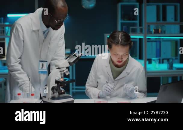 Black male scientist and his Asian female colleague examining sample of ...