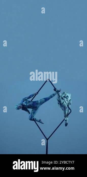 Two acrobats are suspended in a spinning square frame tilted into a ...
