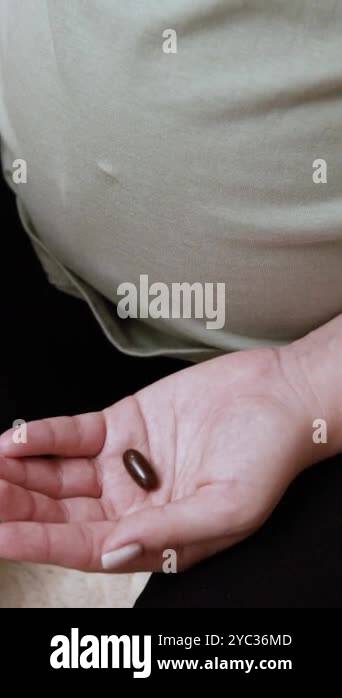 Pregnant woman holds capsule in hand preparing for taking prenatal ...