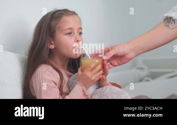 Sick girl drinking juice with straw from glass given by mother while ...