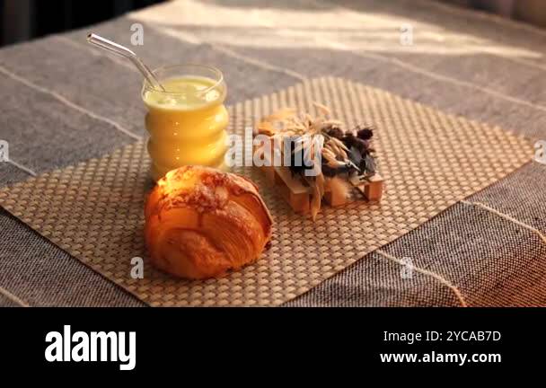Croissant, seeded bread, and glass of yellow juice arranged on woven ...