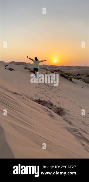 Two people in desert during sunset, one laying on sand while another ...