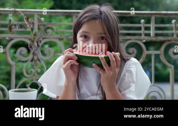 Young girl enjoying a juicy slice of watermelon outdoors, biting into the fresh fruit. Summer ...