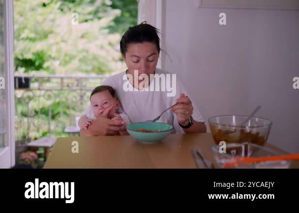Mother eating a meal while holding her baby at the dining table ...