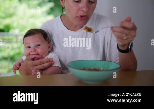 Close-up of a mother holding her baby while eating a meal, focusing on ...