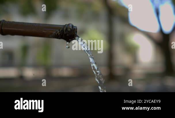 Water flowing from an old metal pipe in a public park, slow motion at ...
