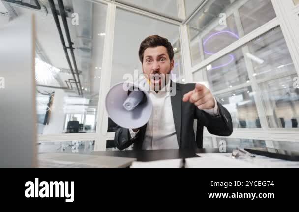 Angry businessman yells into a megaphone in his office. He points his ...