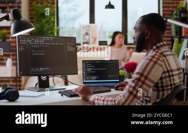 Male coder works from home typing code on a laptop in a modern living room. African american IT ...