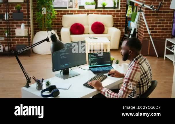 Young man seen programming software code on his laptop in a sleek home ...