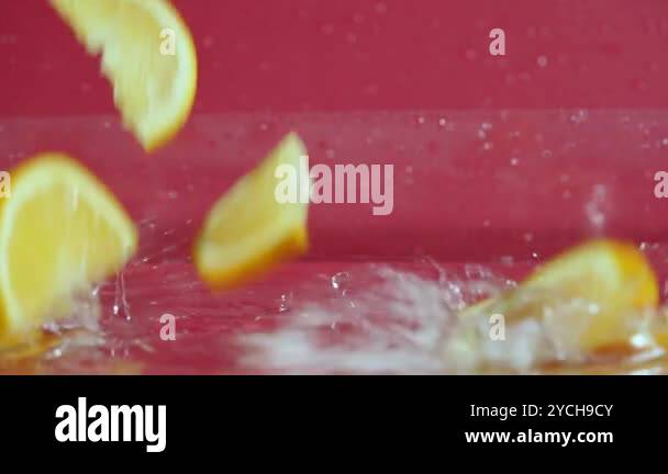 Close up of fresh lemon slices splashing on red background. Macro of sliced lemon dropping and ...