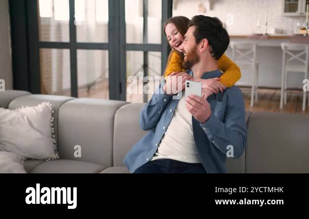 Cheerful Caucasian daughter little child surprise hug embracing distracting dad parent male ...