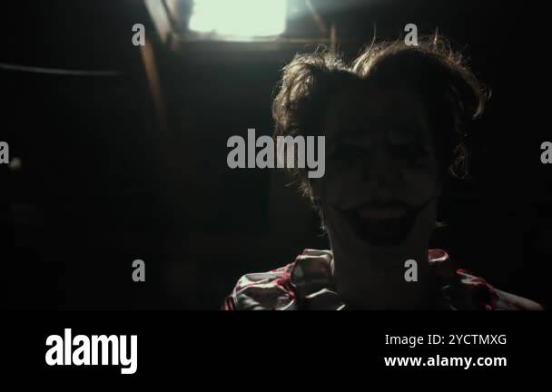 Scary mad clown at rooftop in darkness. Crazy creepy killer man dressed ...