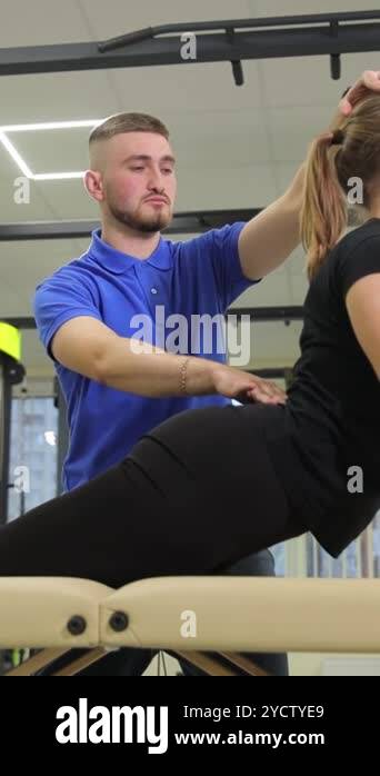 A fitness trainer helps a female client with leg stretches on a gym ...