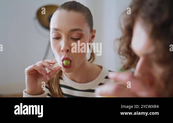 Relaxed girl eating grape in bright kitchen with curly boyfriend ...