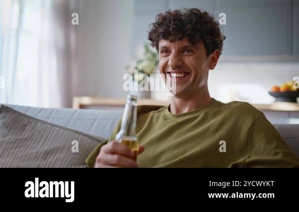 Laughing man enjoy tv show relaxing with beer at cozy home couch ...