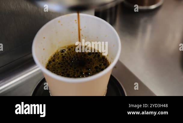 A close-up shot of freshly brewed coffee pouring into a paper cup from ...