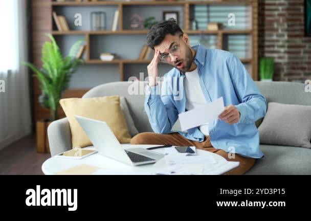 Frustrated young adult man looking at large utility bills sitting on ...