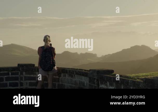 A solo female traveler overlooks a serene landscape from a stone ...