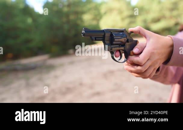 A person firing a revolver at an outdoor shooting range, with smoke ...