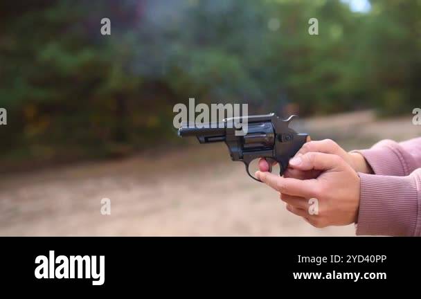 A person firing a revolver at an outdoor shooting range, with smoke ...
