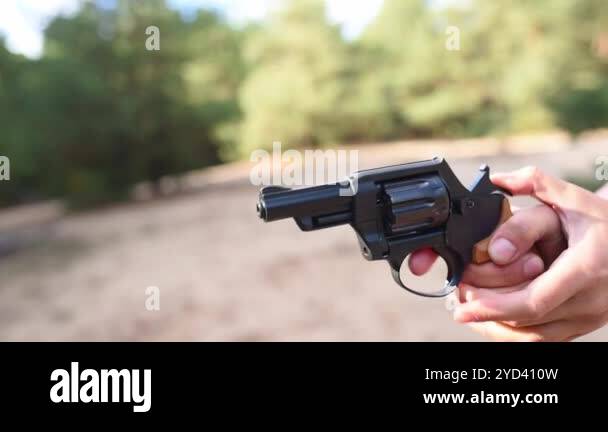 A person firing a revolver at an outdoor shooting range, with smoke ...