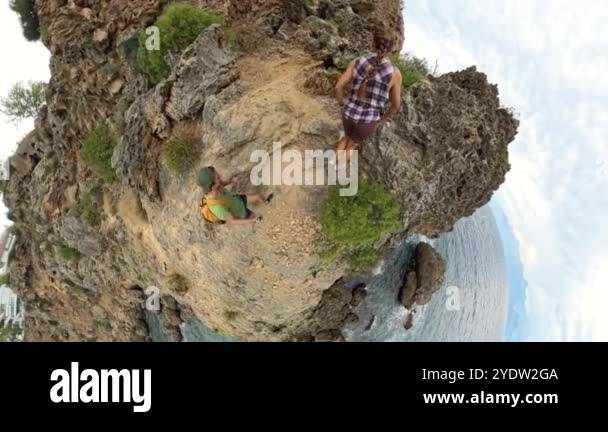 A Man and Woman stand on a rocky cliff overlooking the sea, surrounded ...