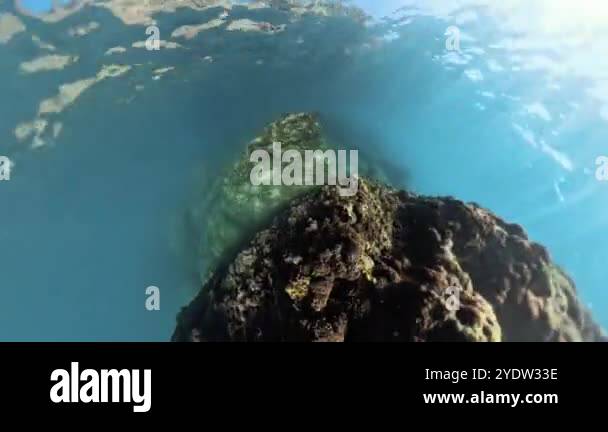 A diver swims deeper, navigating between rocks, as the water creates a ...