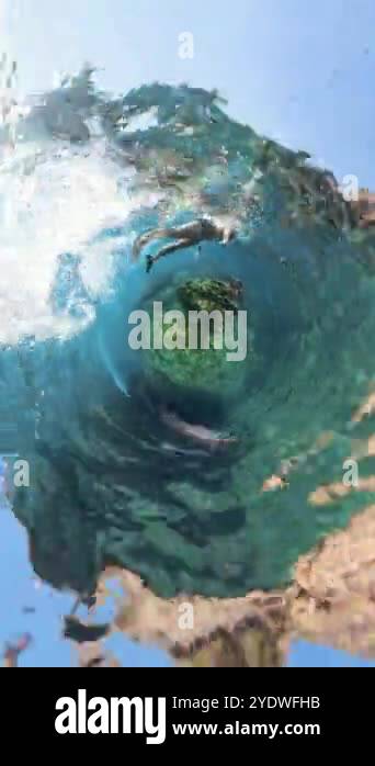 Vertical video. A diver in the water, seen in a Tiny Planet effect ...