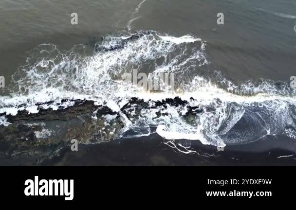 An aerial shot capturing the powerful ocean waves crashing against dark ...